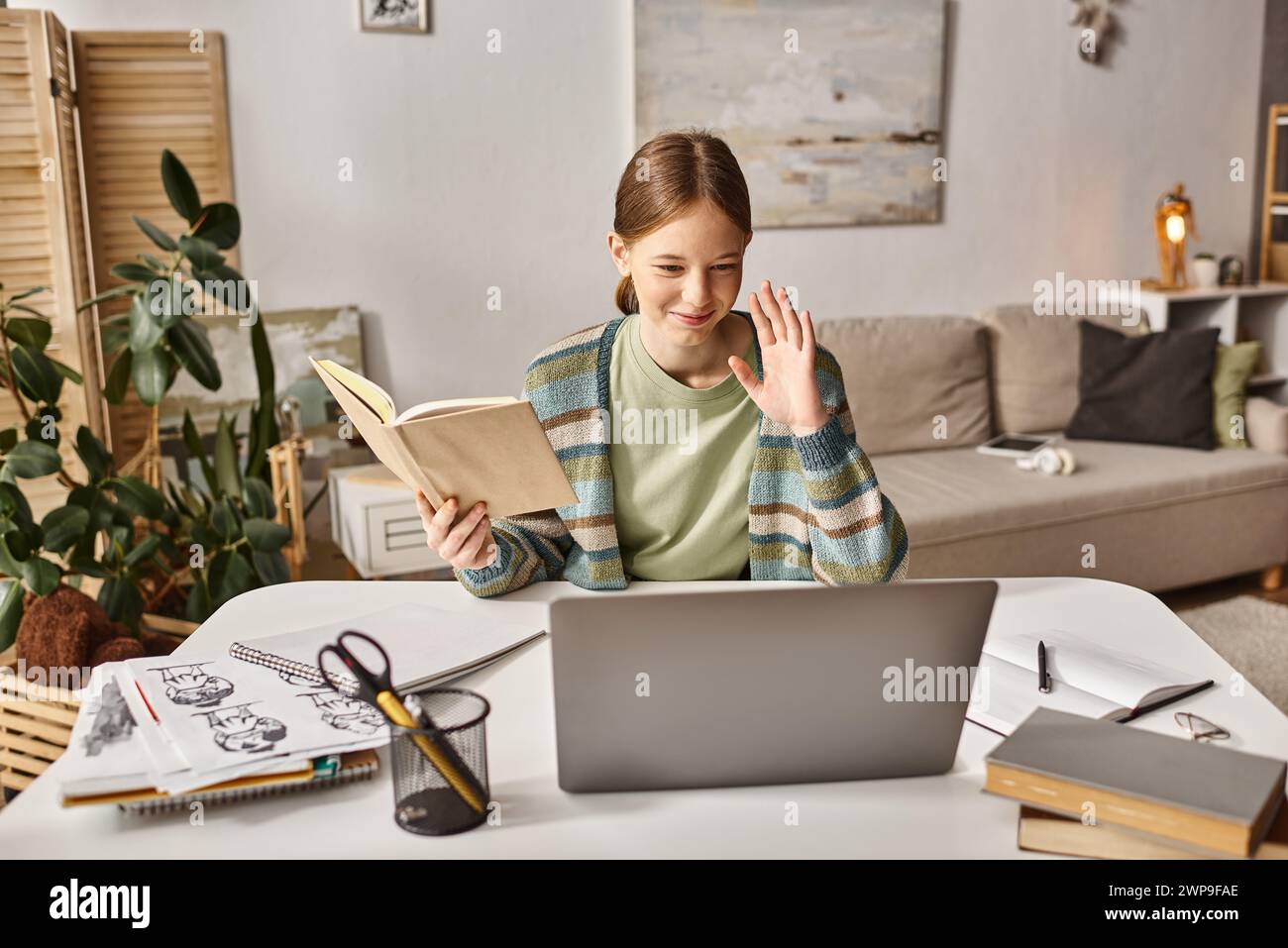 happy gen z girl holding book while using a laptop during video call at ...