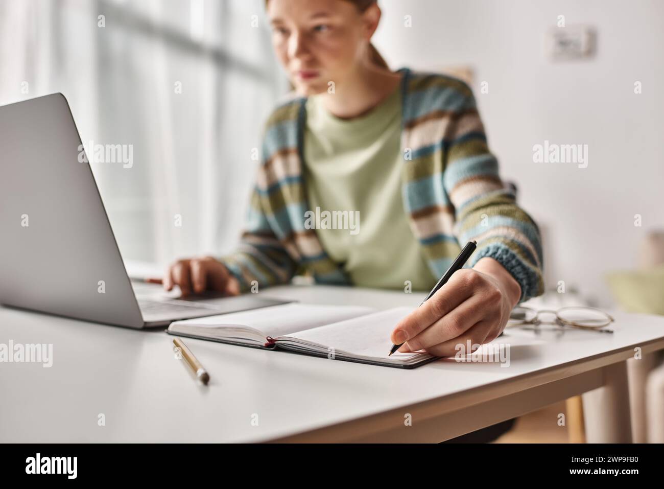 Focused teenager doing homework on laptop in a home environment, focus ...