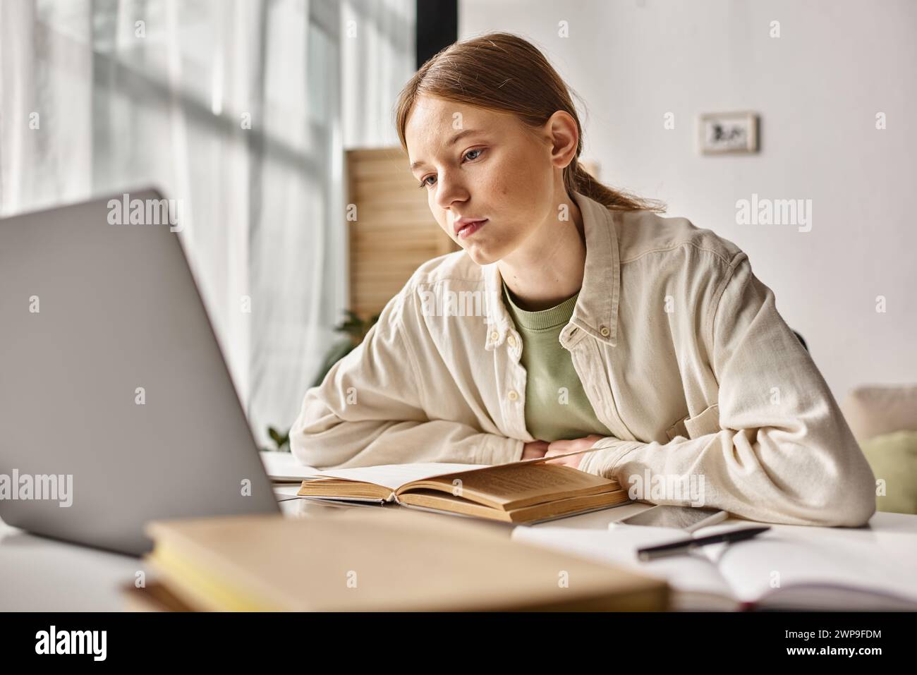 Focused teenager doing homework on laptop in a home environment, focus ...