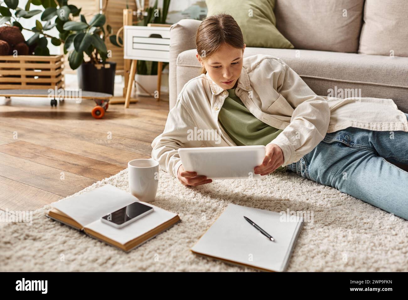 teenage girl holding tablet near cup of tea while making her homework, digital native concept ...