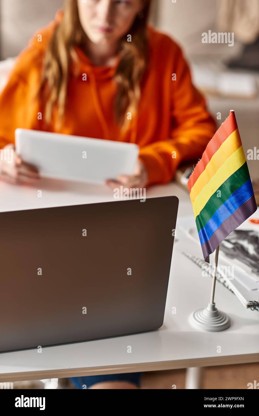 focus of lgbtq pride flag and laptop on desk near blurred teenage girl ...