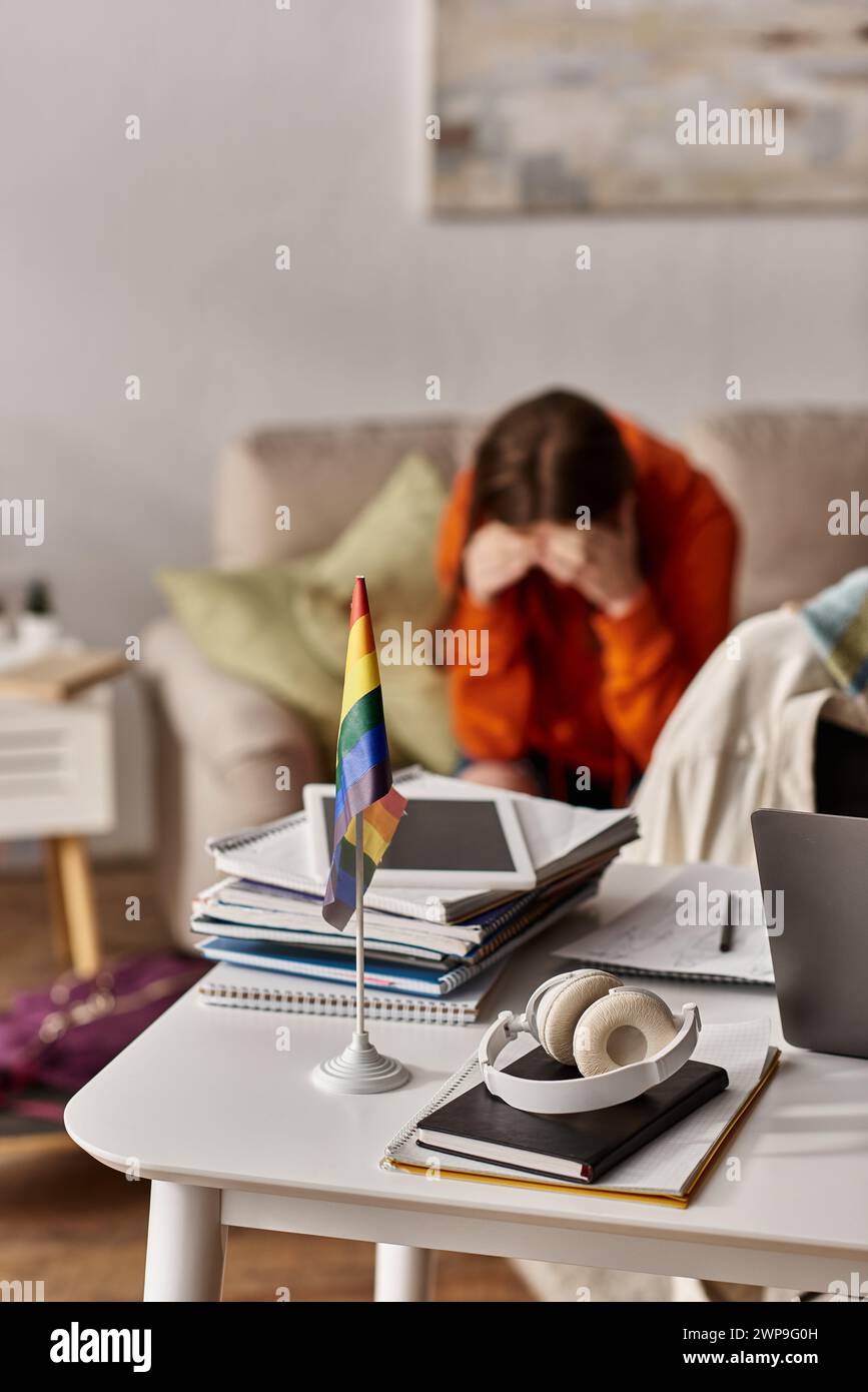 focus on lgbtq pride flag on messy working desk with devices, blurred ...