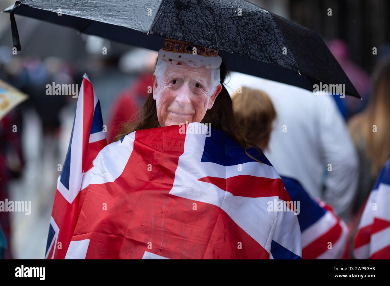 A mask of King Charles III is seen on the head of a pedestrian wearing ...
