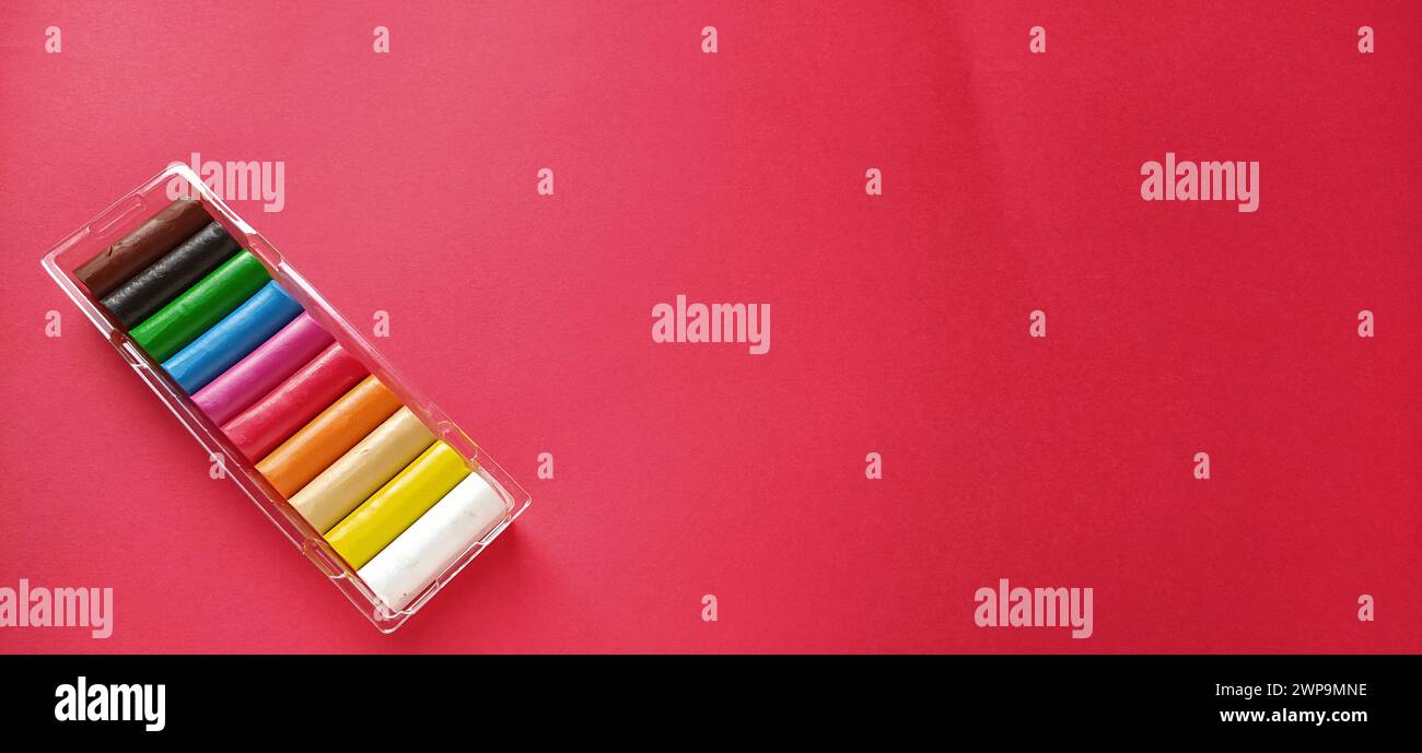 Multi-colored new plasticine in plastic packaging on a red background ...