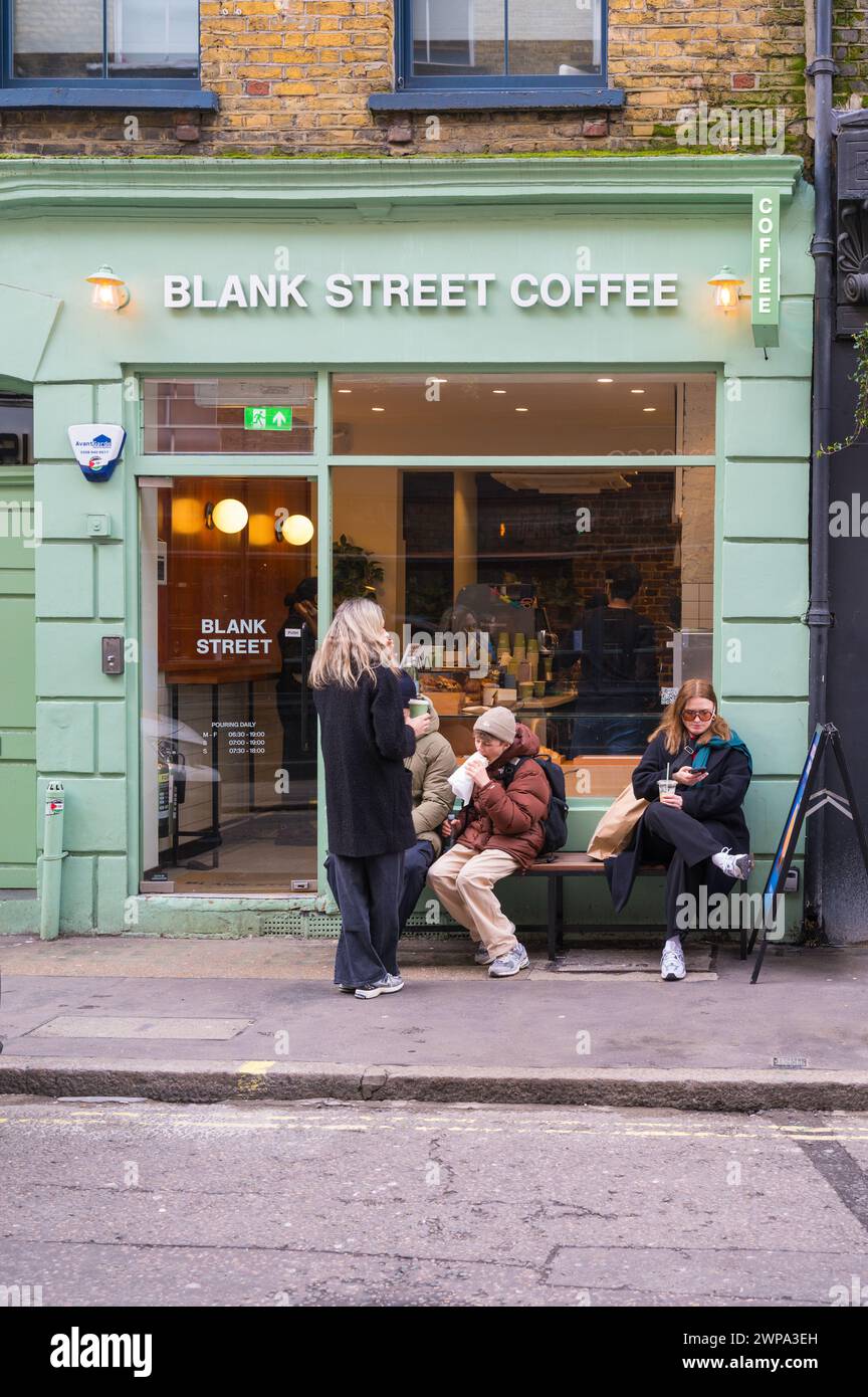 Group of young people enjoying refreshments seated on bench outside ...