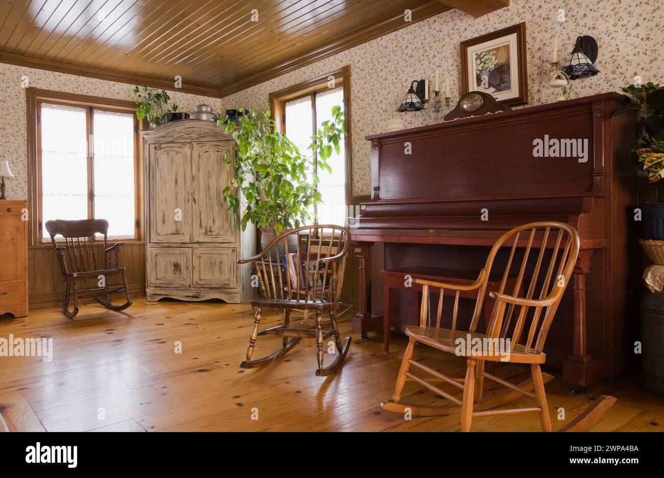 Rocking chairs, upright piano and antique armoire in living room with ...