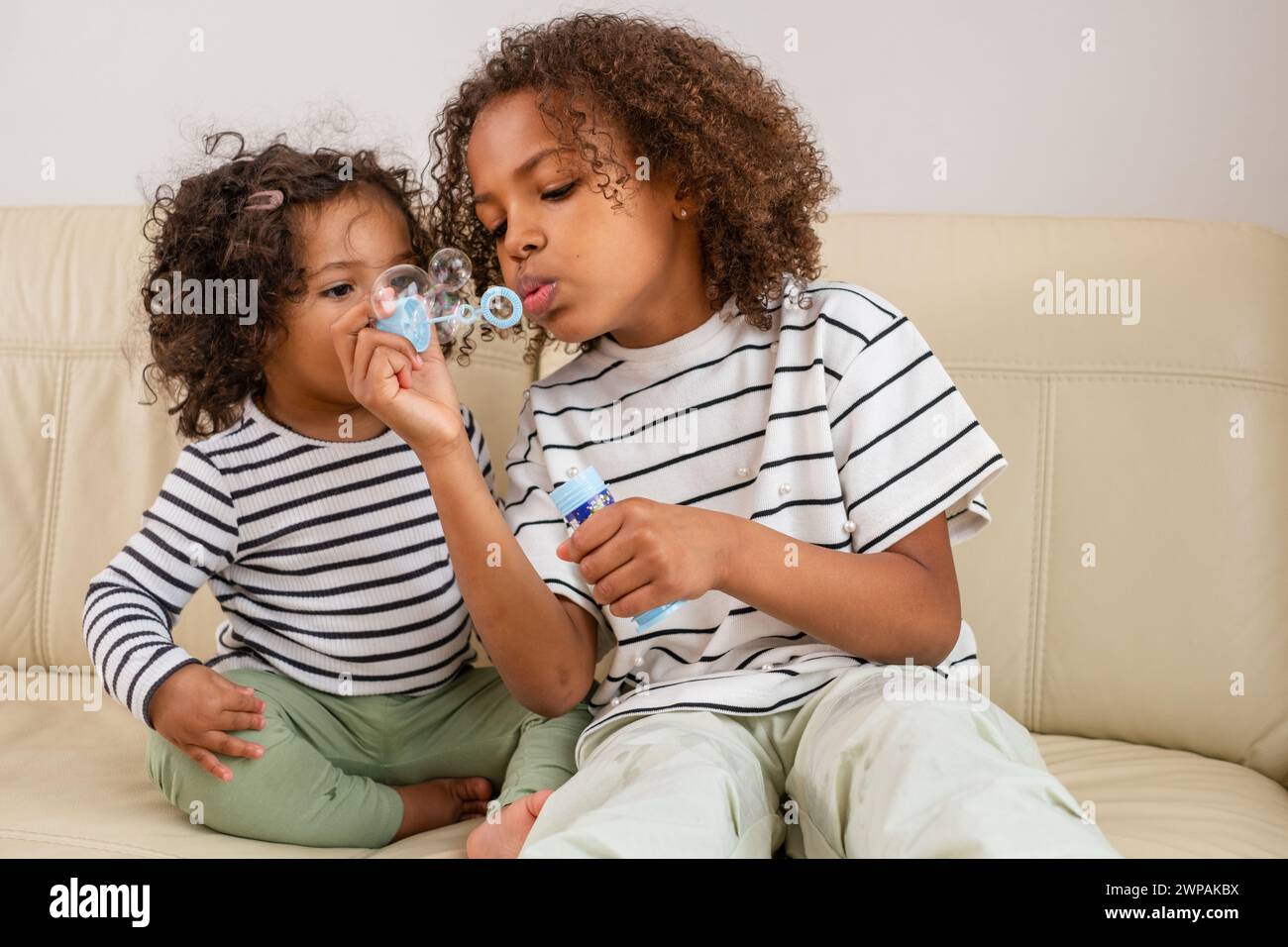 Two young mixed race sisters in striped attire play with bubbles on a ...