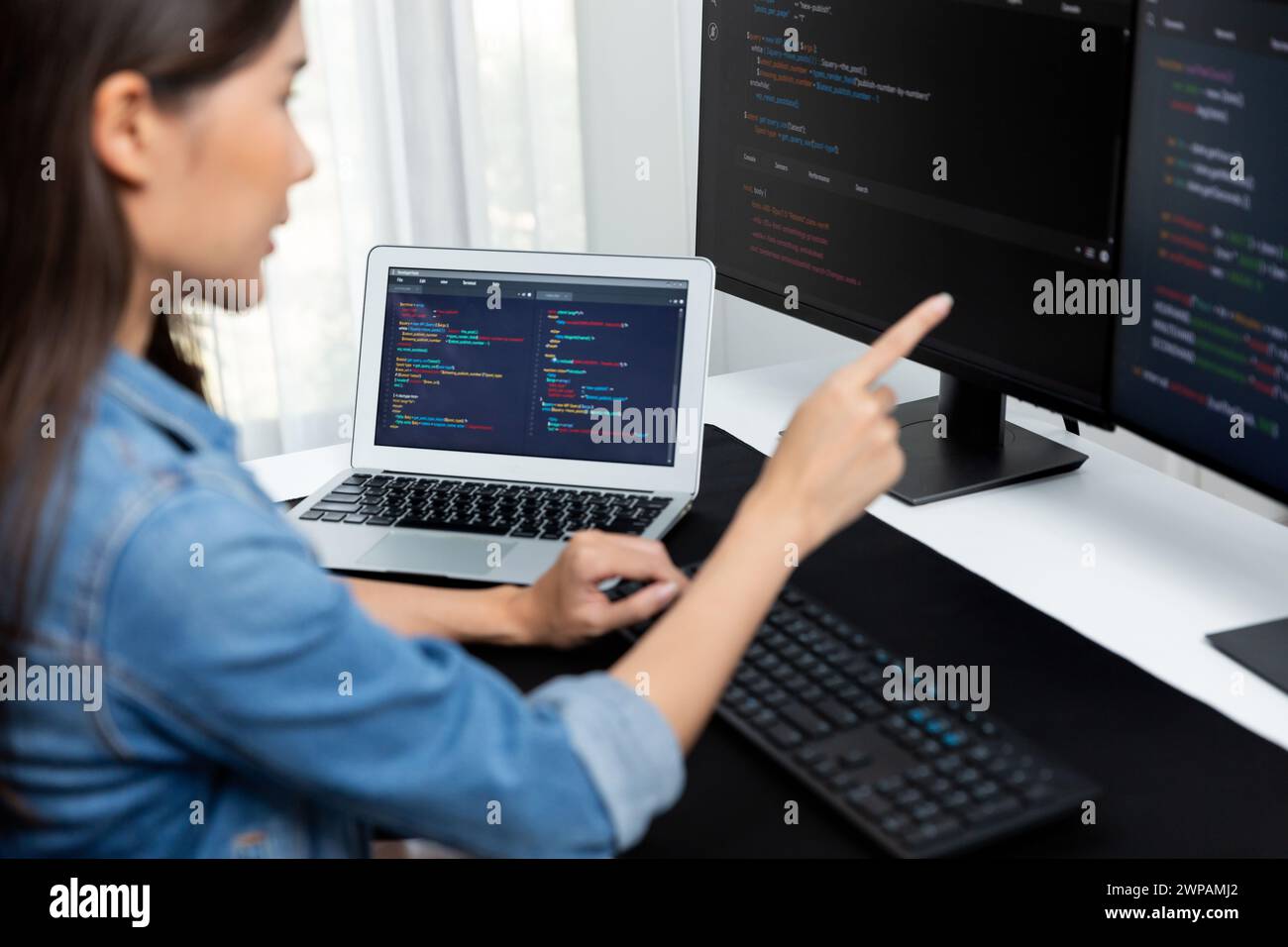 Young Asian girl of IT developer pointing online information on pc with coding program data ...