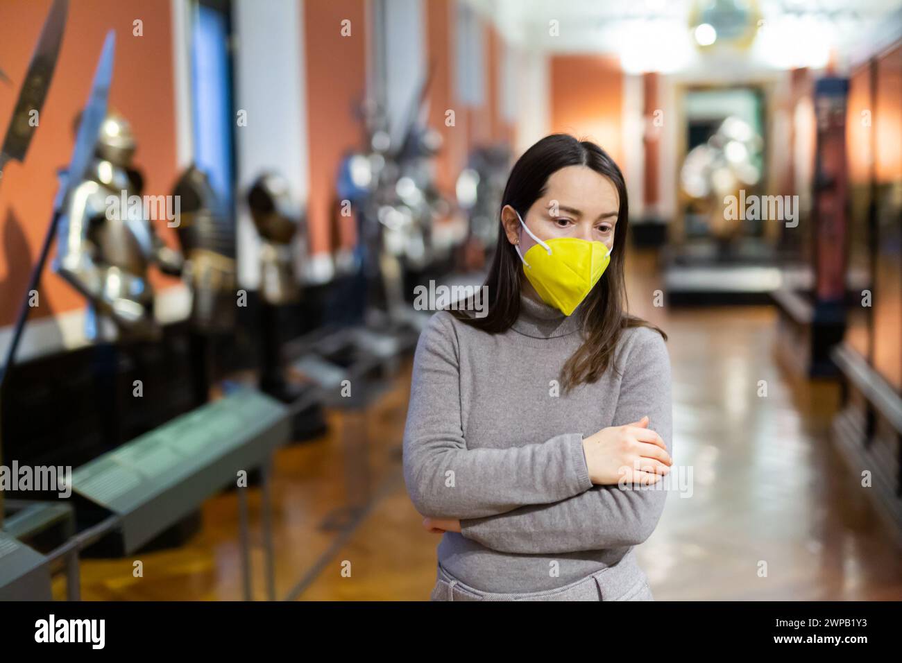 Woman in protective mask viewing collection of medieval armor in museum ...