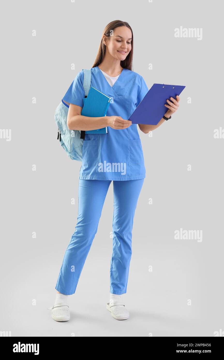 Female medical intern with clipboard on light background Stock Photo ...