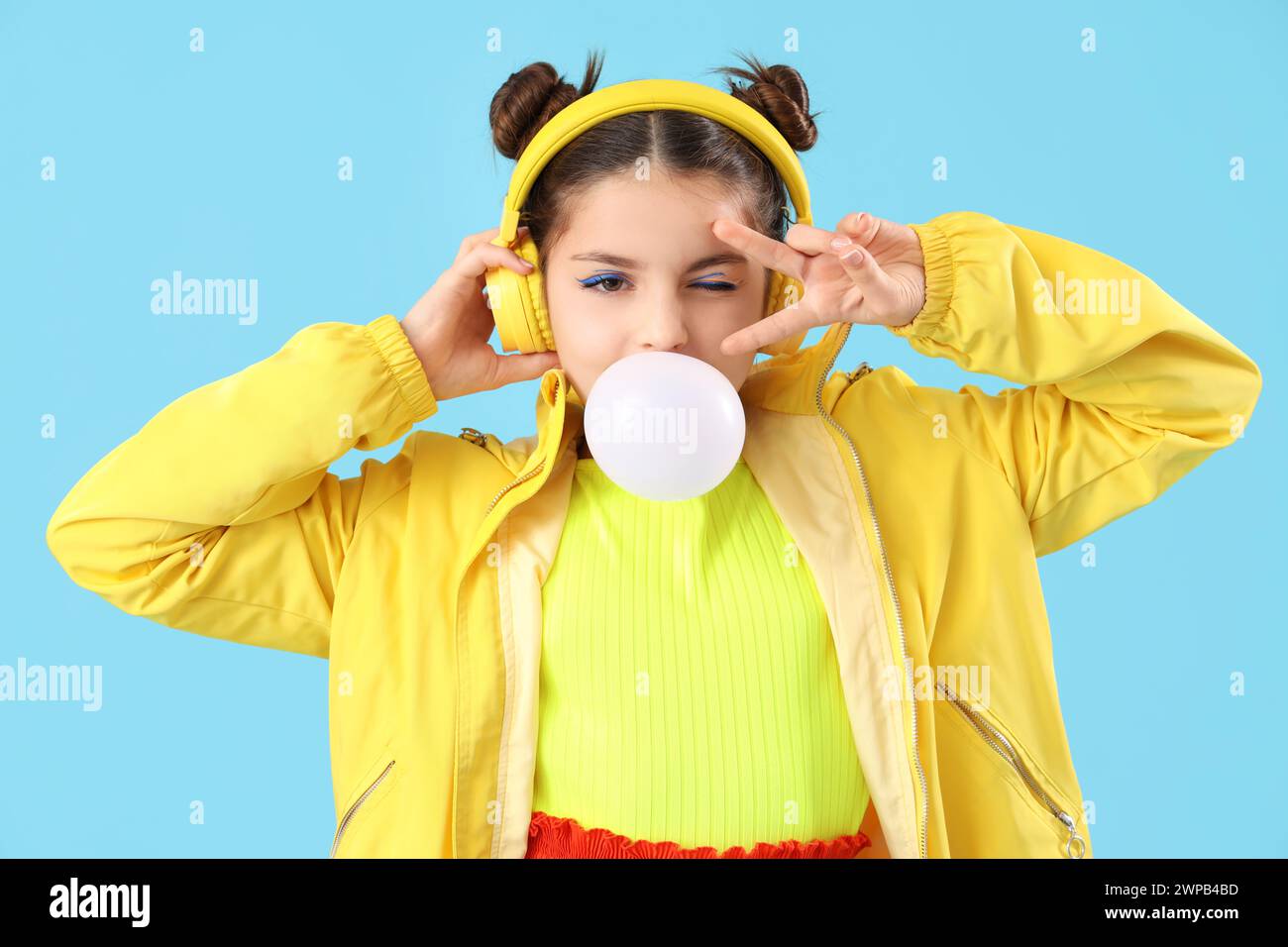 Trendy girl blowing bubble gum while showing victory gesture on blue ...