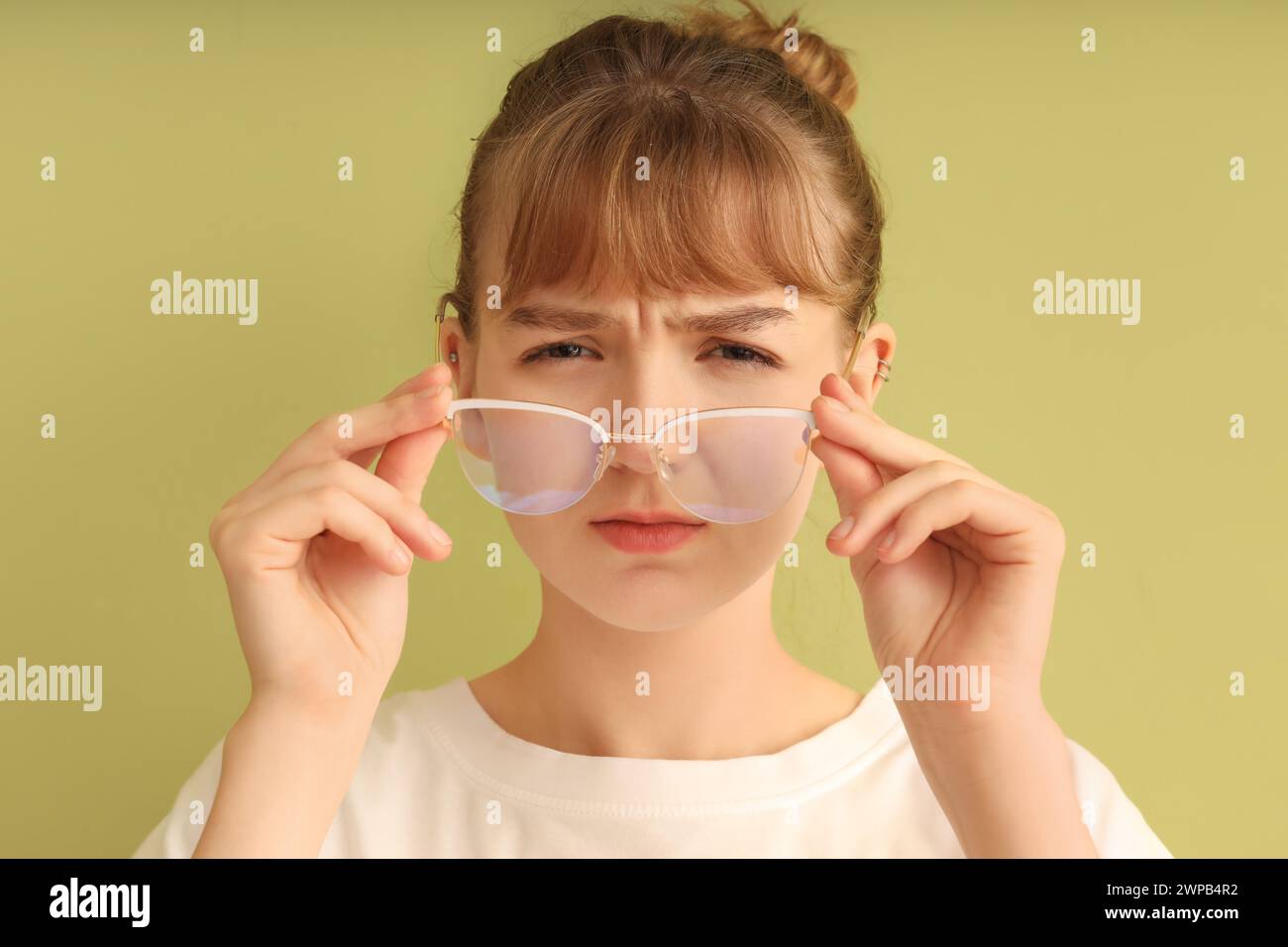 Young woman with eyeglasses squinting on green background, closeup ...