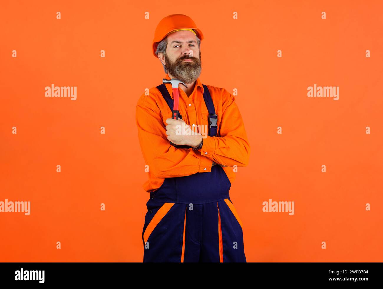 Builder in construction overalls and hard hat with hammer. Bearded man ...