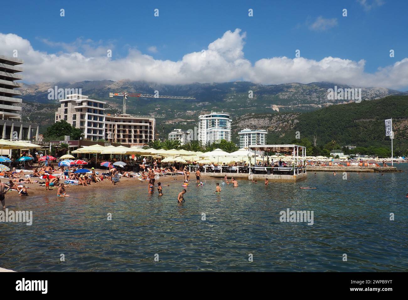 Budva, Montenegro 08.15.22 Pebble beach near mountains. Beach umbrellas, cafes, deck chairs ...
