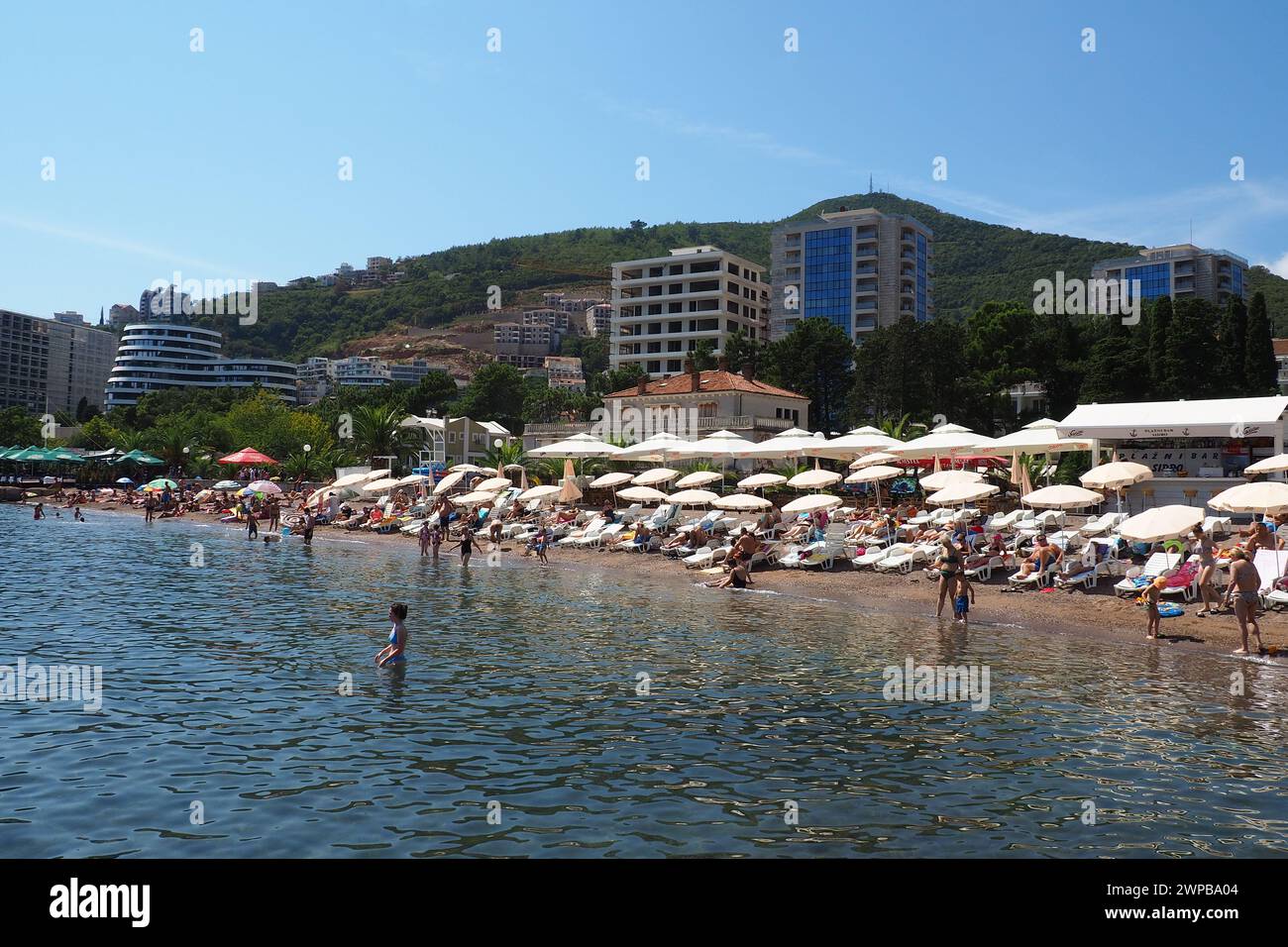 Budva, Montenegro 08.15.22 Pebble beach near mountains. Beach umbrellas, cafes, deck chairs ...