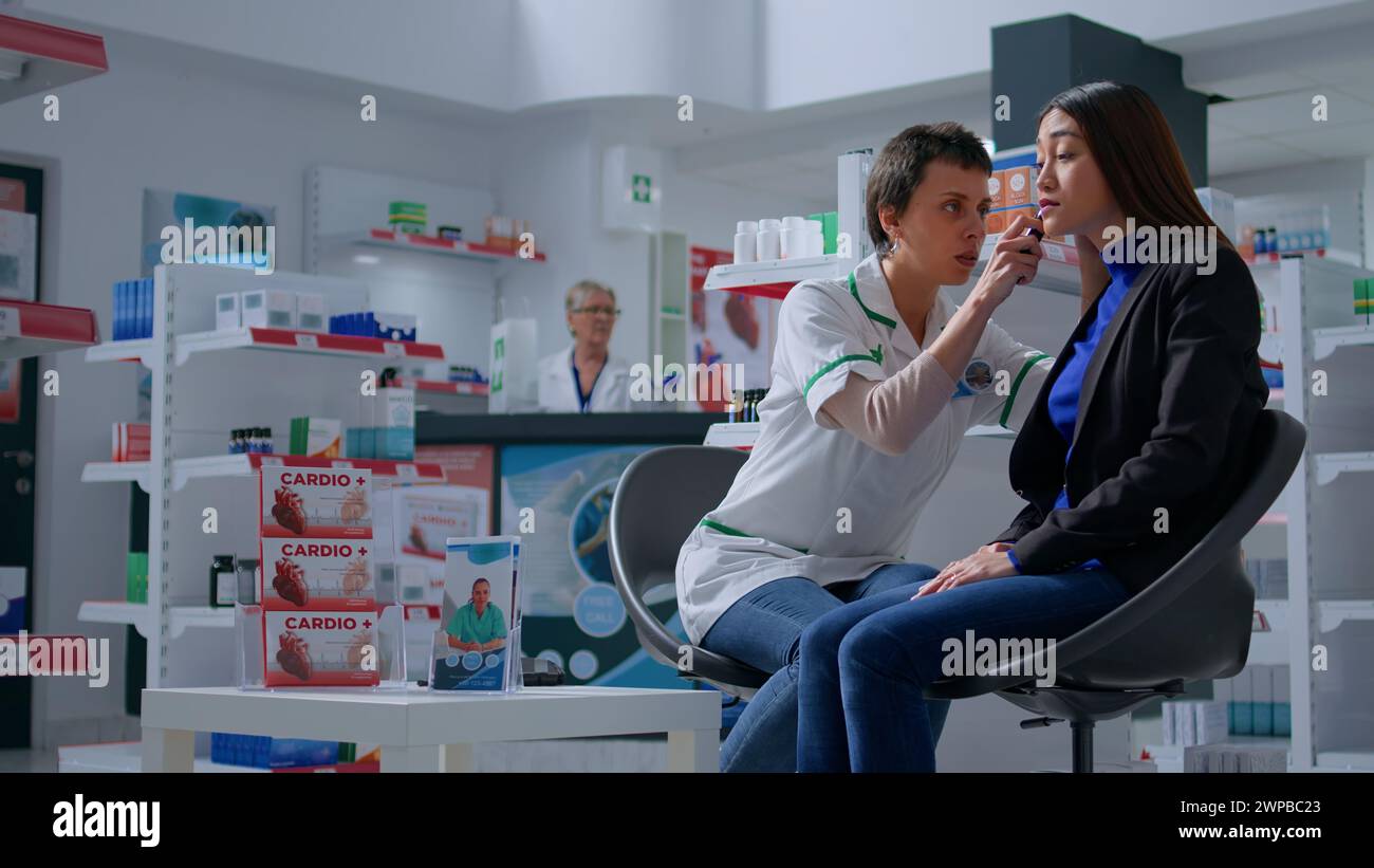 Pharmacist in drugstore doing annual patient checkup, using otoscope to ...