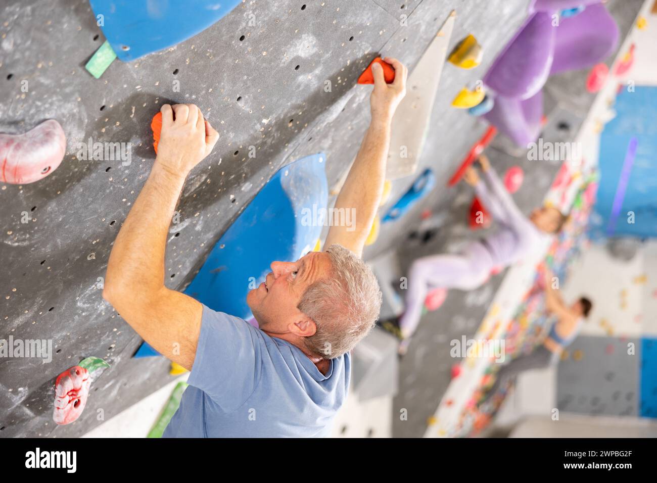 Male mountaineer climbing artificial rock wall without belay indoors ...
