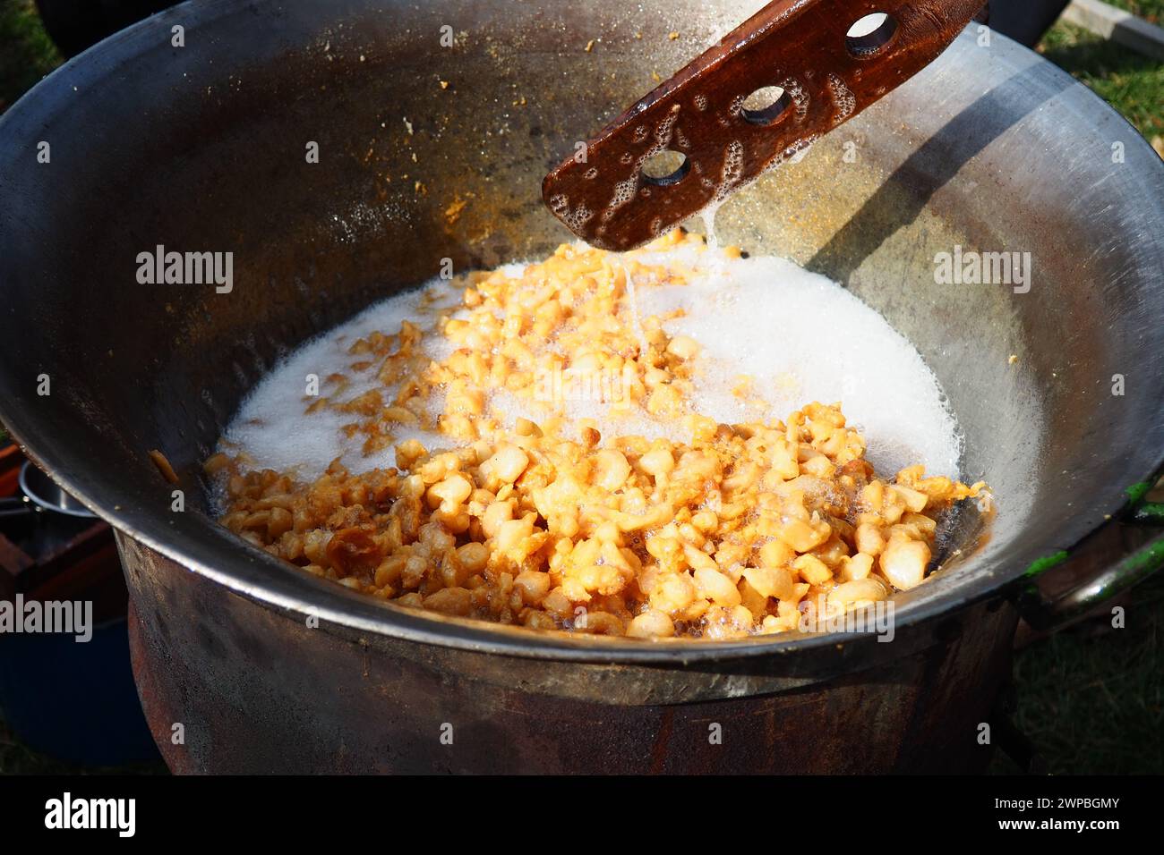 Stirring fat in a large vat on firewood. Pork rinds rendered, fried in ...