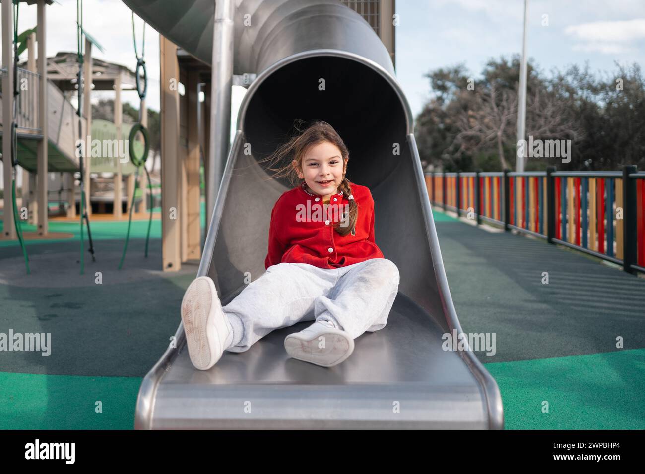A happy child sits at the top of a slide in a playground, ready for fun ...