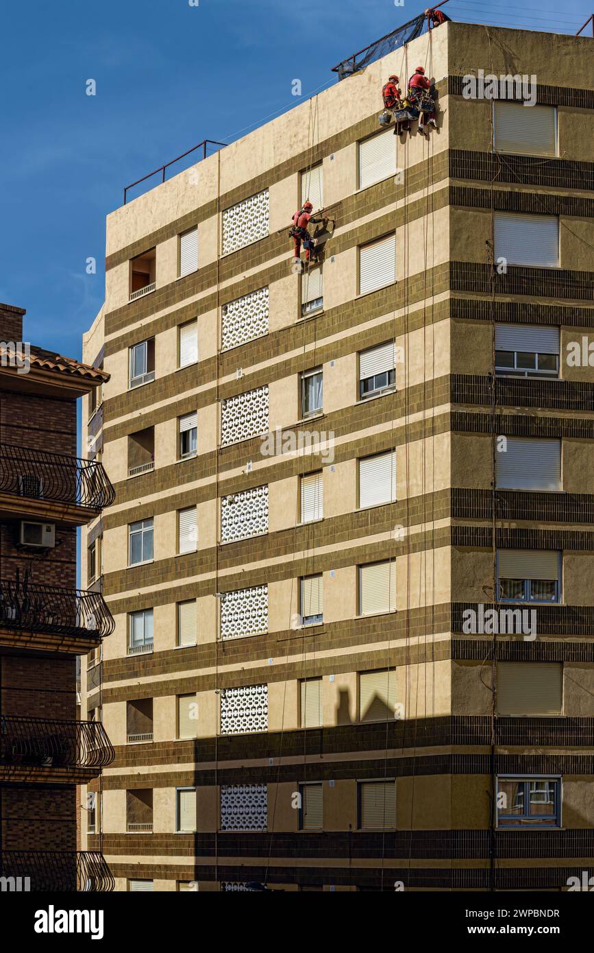 Workers hanging on ropes repainting the facade wall of a typical ...