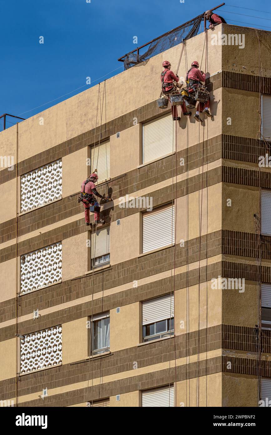 Workers hanging on ropes repainting the facade wall of a typical ...