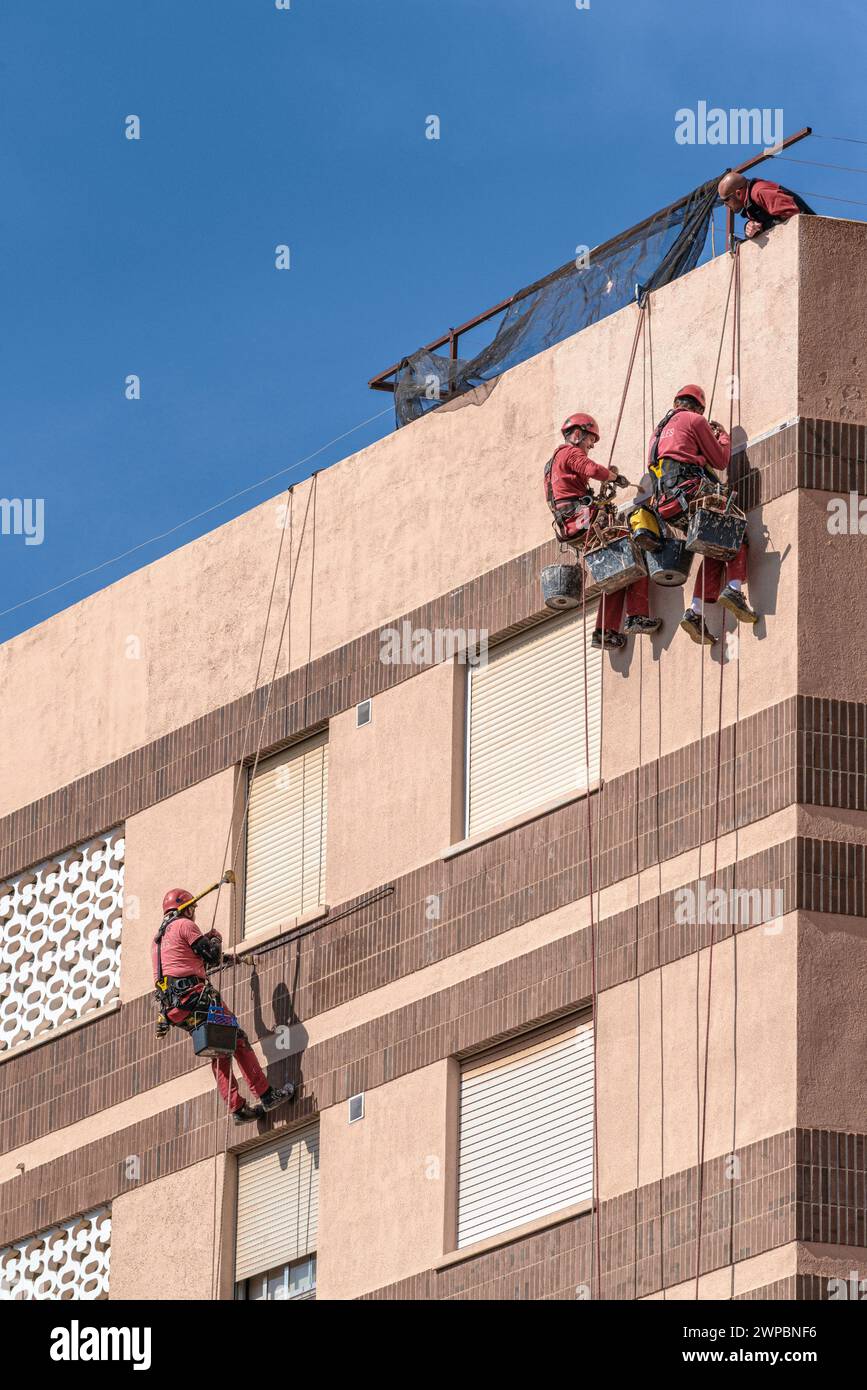 Workers hanging on ropes repainting the facade wall of a typical ...