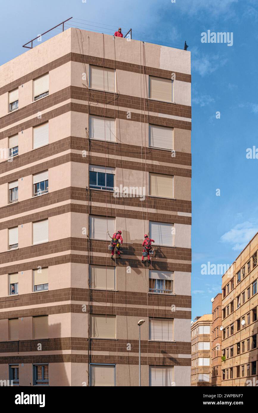 Workers hanging on ropes repainting the facade wall of a typical ...