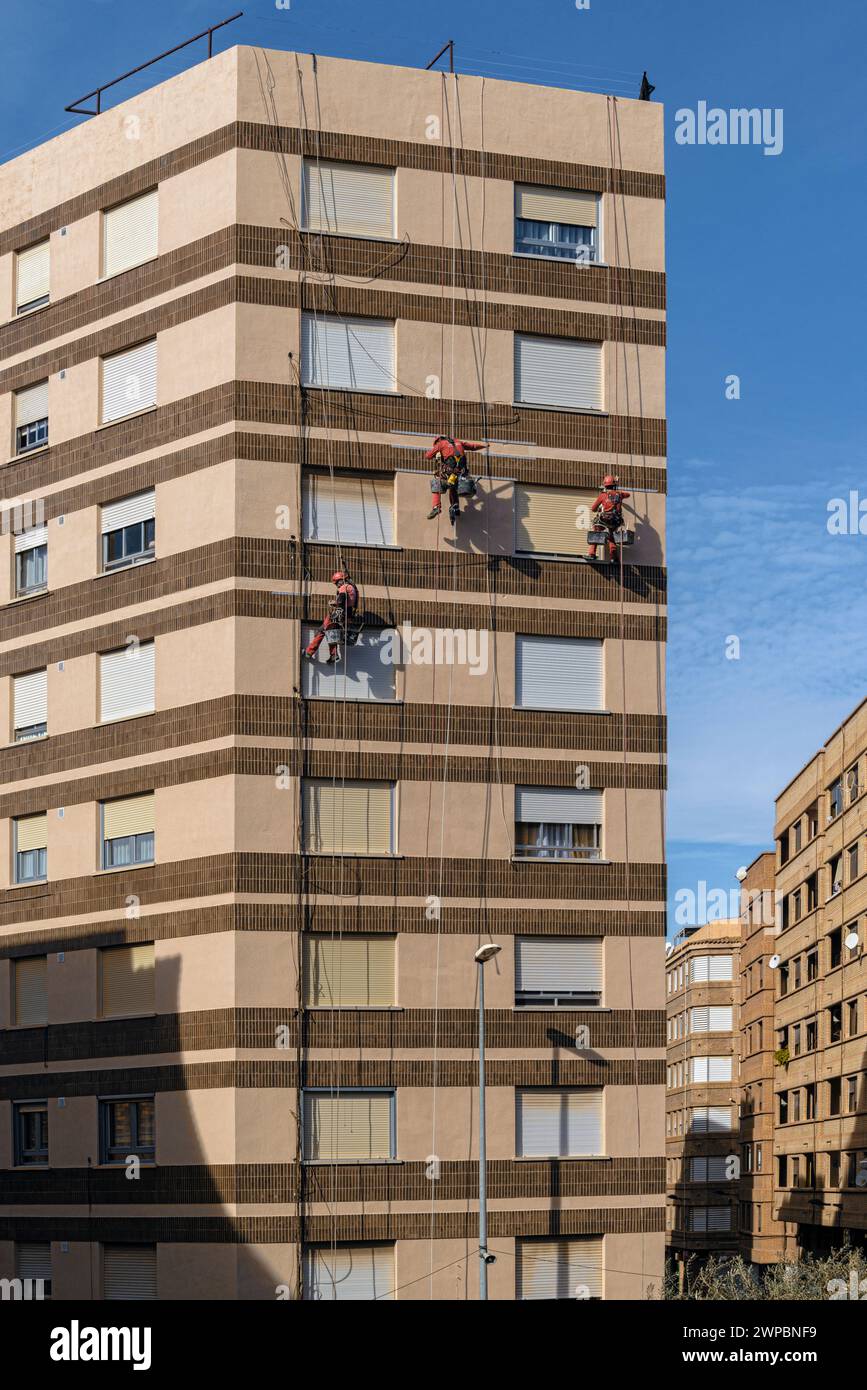 Workers hanging on ropes repainting the facade wall of a typical ...