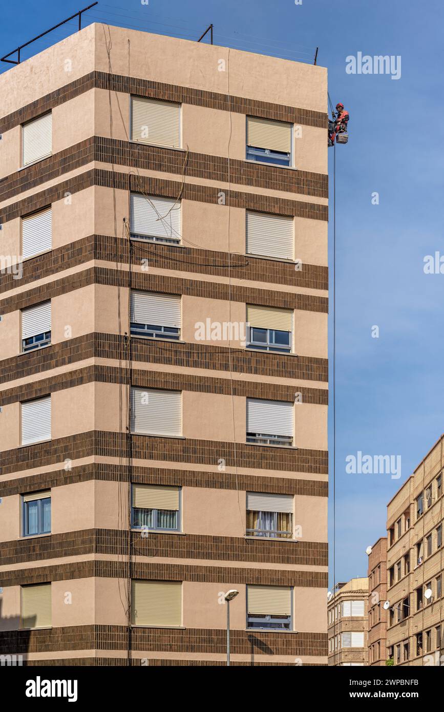 Workers hanging on ropes repainting the facade wall of a typical ...