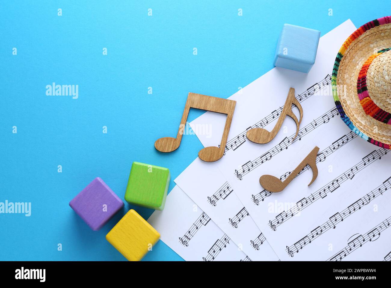 Baby songs. Music sheets, wooden notes, cubes and hat on light blue ...