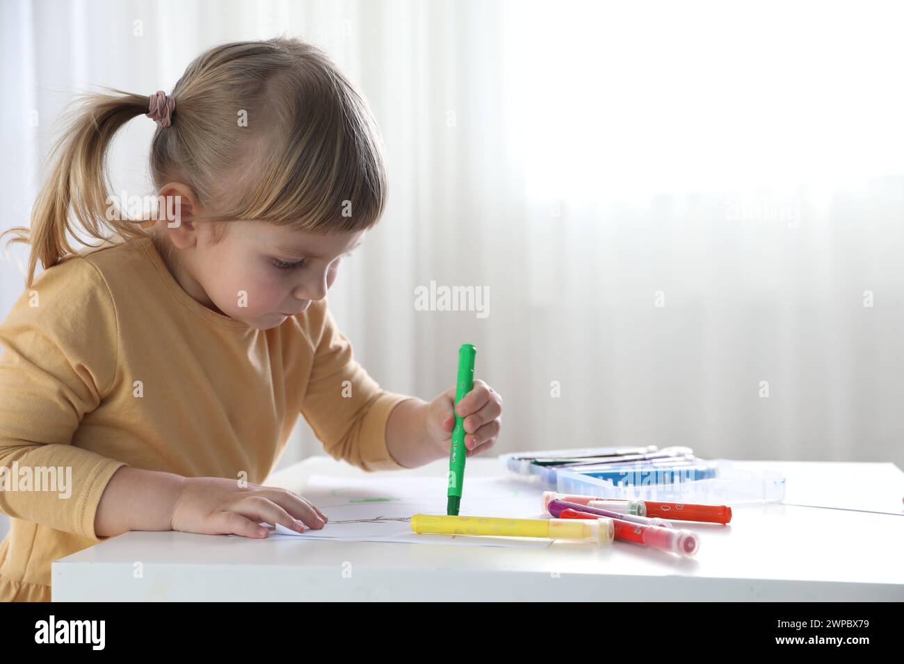 Cute little girl drawing with marker at white table indoors. Child`s ...