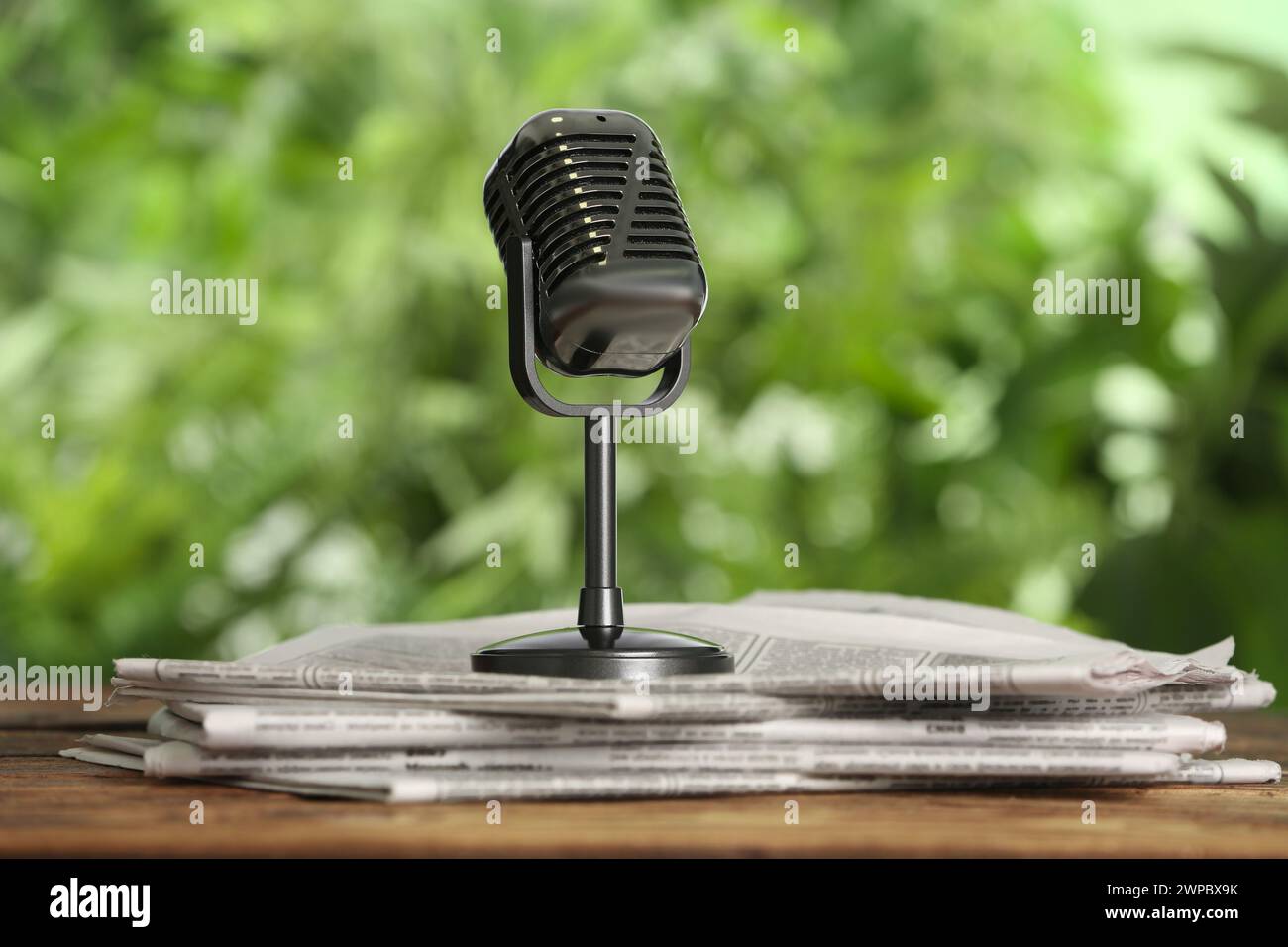 Newspapers and vintage microphone on wooden table against blurred green ...