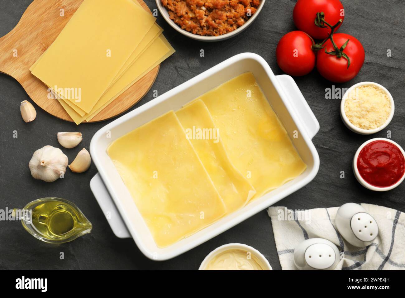 Cooking lasagna. Pasta sheets in baking tray and products on dark ...