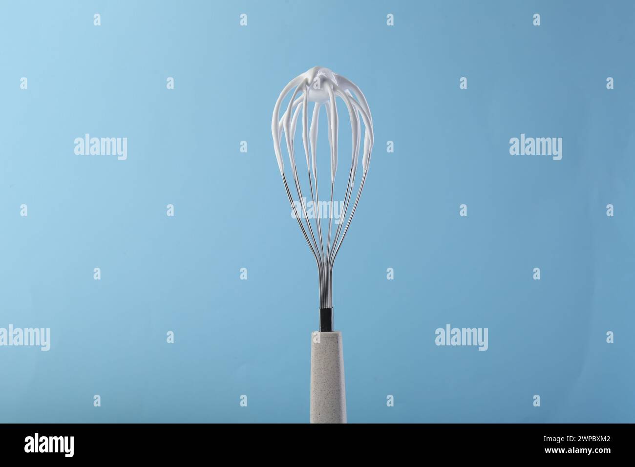 Whisk with whipped cream on light blue background Stock Photo - Alamy