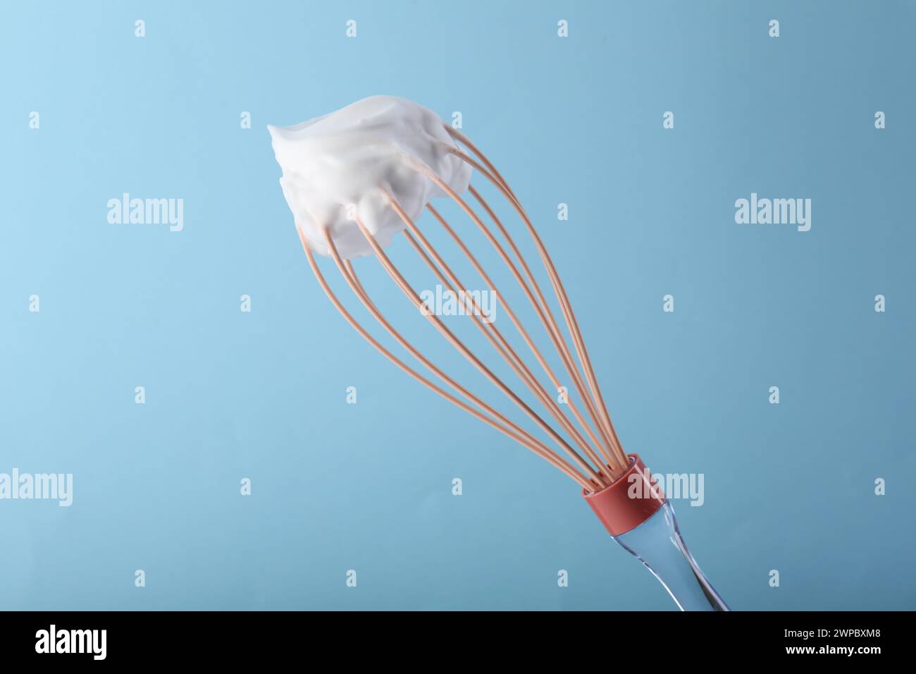 Whisk with whipped cream on light blue background Stock Photo - Alamy