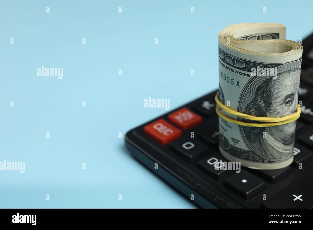 Money exchange. Rolled dollar banknotes and calculator on light blue ...