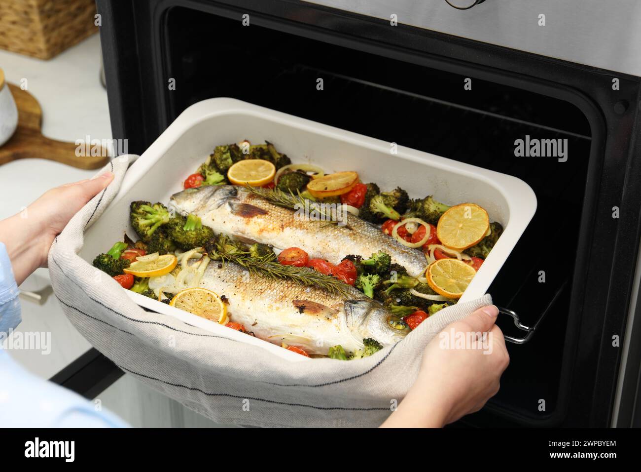 Woman taking baking dish with delicious fish and vegetables from oven ...