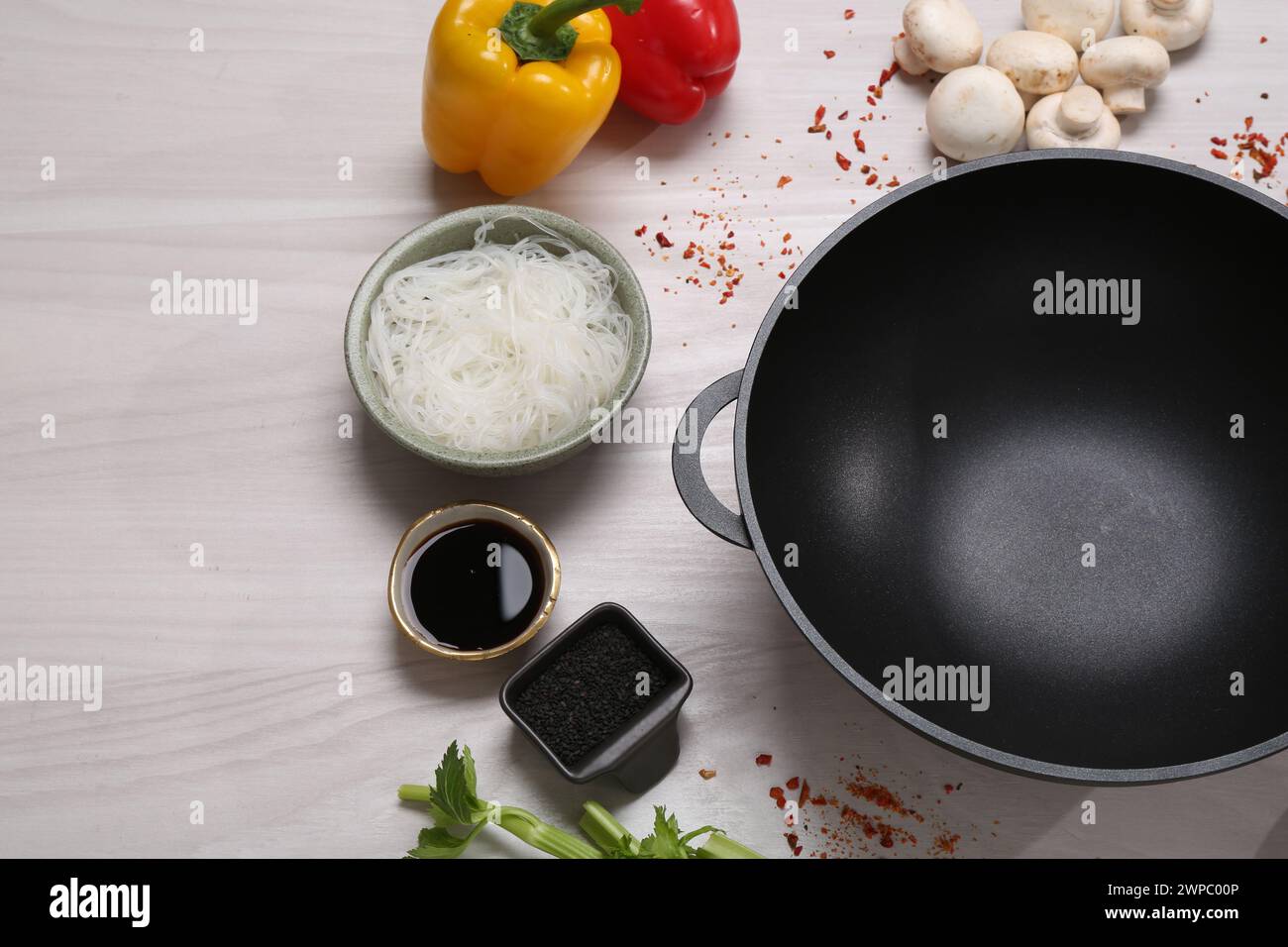 Wok and different products on white wooden table, above view. Space for ...