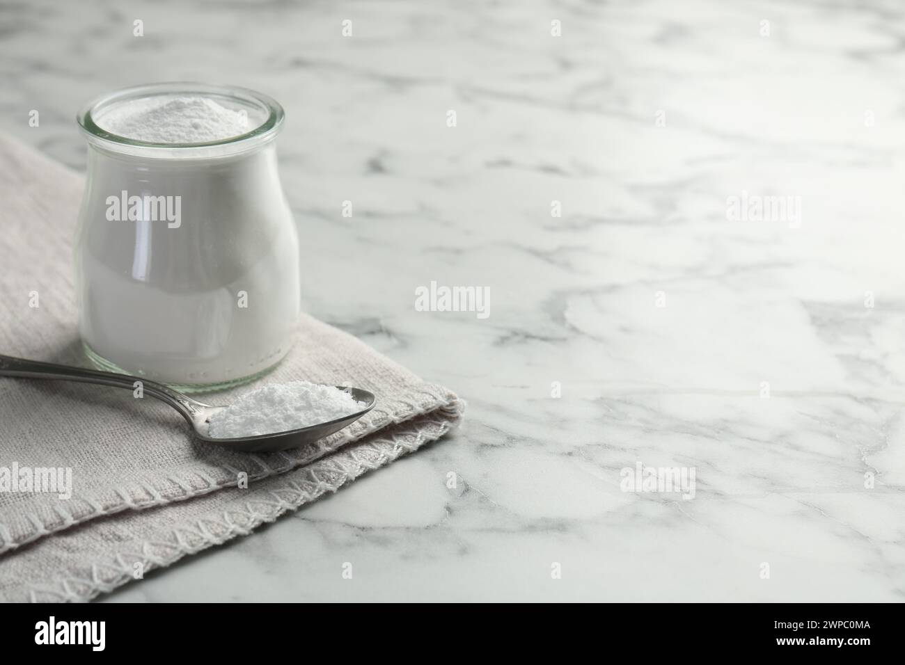 Baking powder in jar and spoon on white marble table, space for text ...