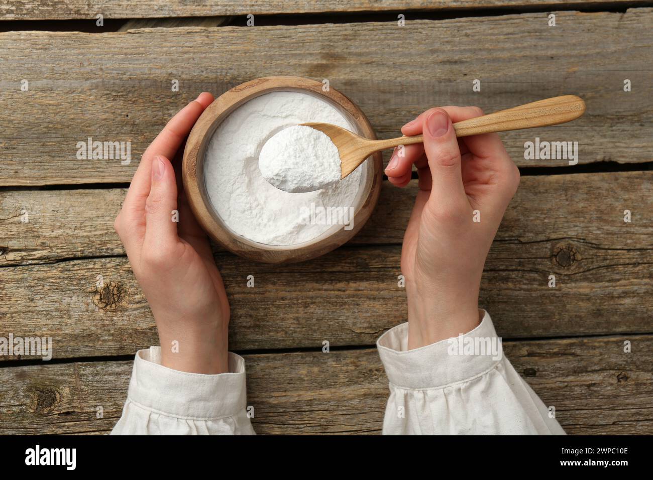 Woman taking baking powder with spoon from bowl at wooden table, top ...