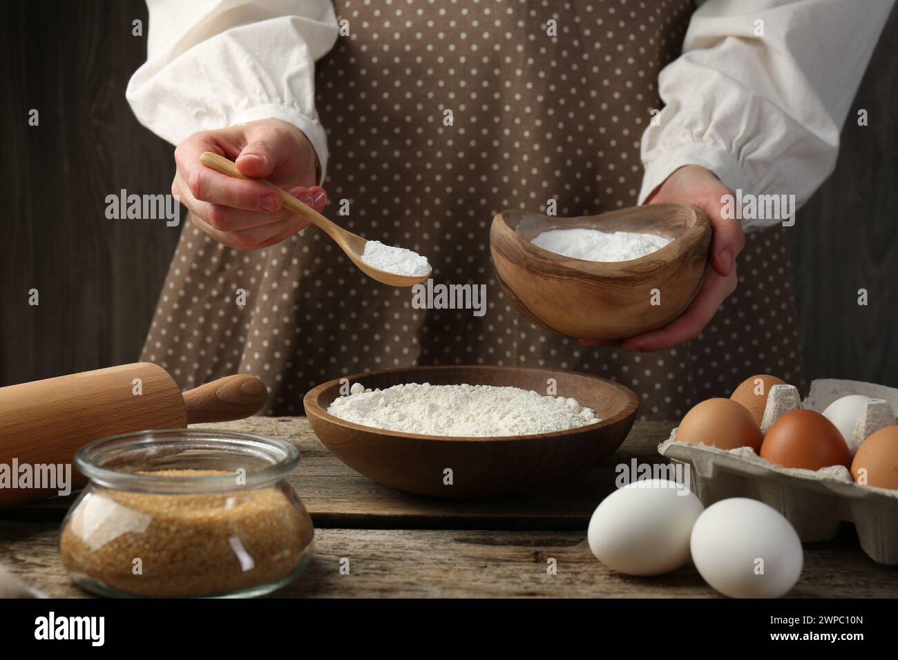 Making dough. Woman adding baking powder to flour at wooden table ...