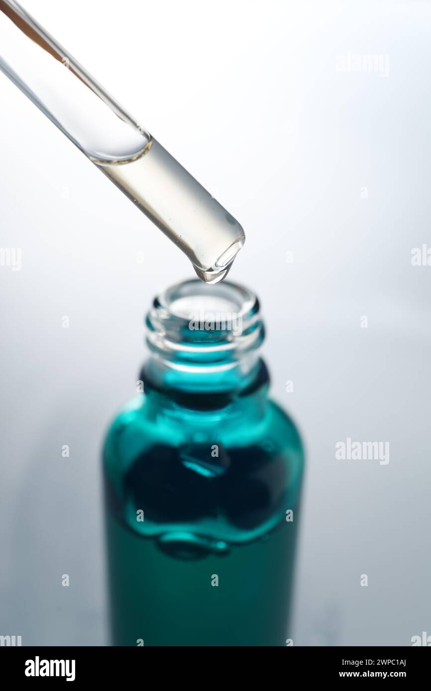 Dripping moisturizing serum from pipette into bottle on light grey ...