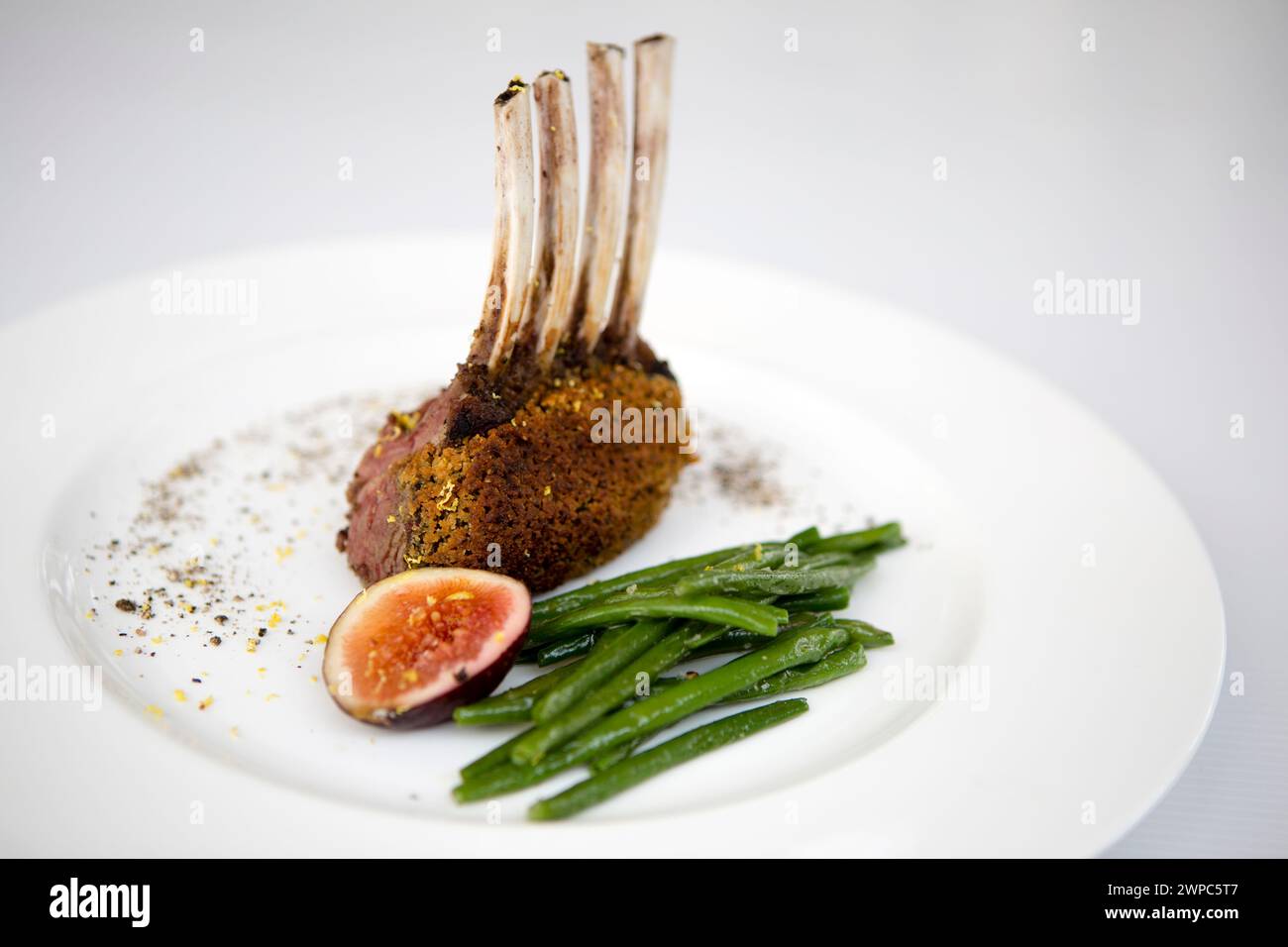 Roasted spring lamb rack with fig and green beans on a white dish Stock ...