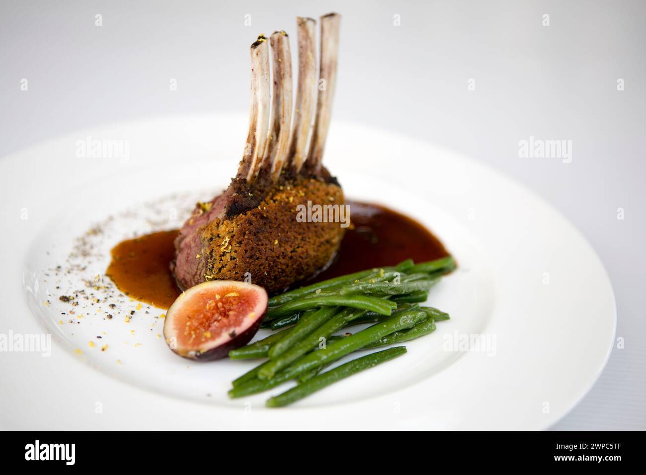 Roasted spring lamb rack with fig and green beans on a white dish Stock ...