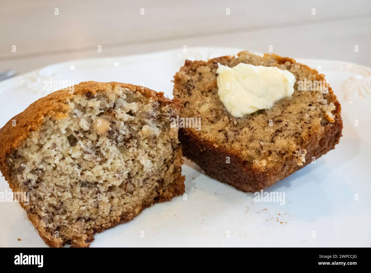 Home-baked banana nut muffin split in half with butter on a white plate ...