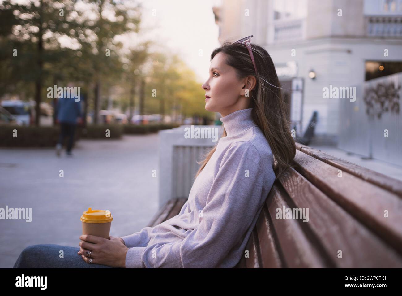 Woman drinks from cup on wooden bench. She is wearing a white shirt ...