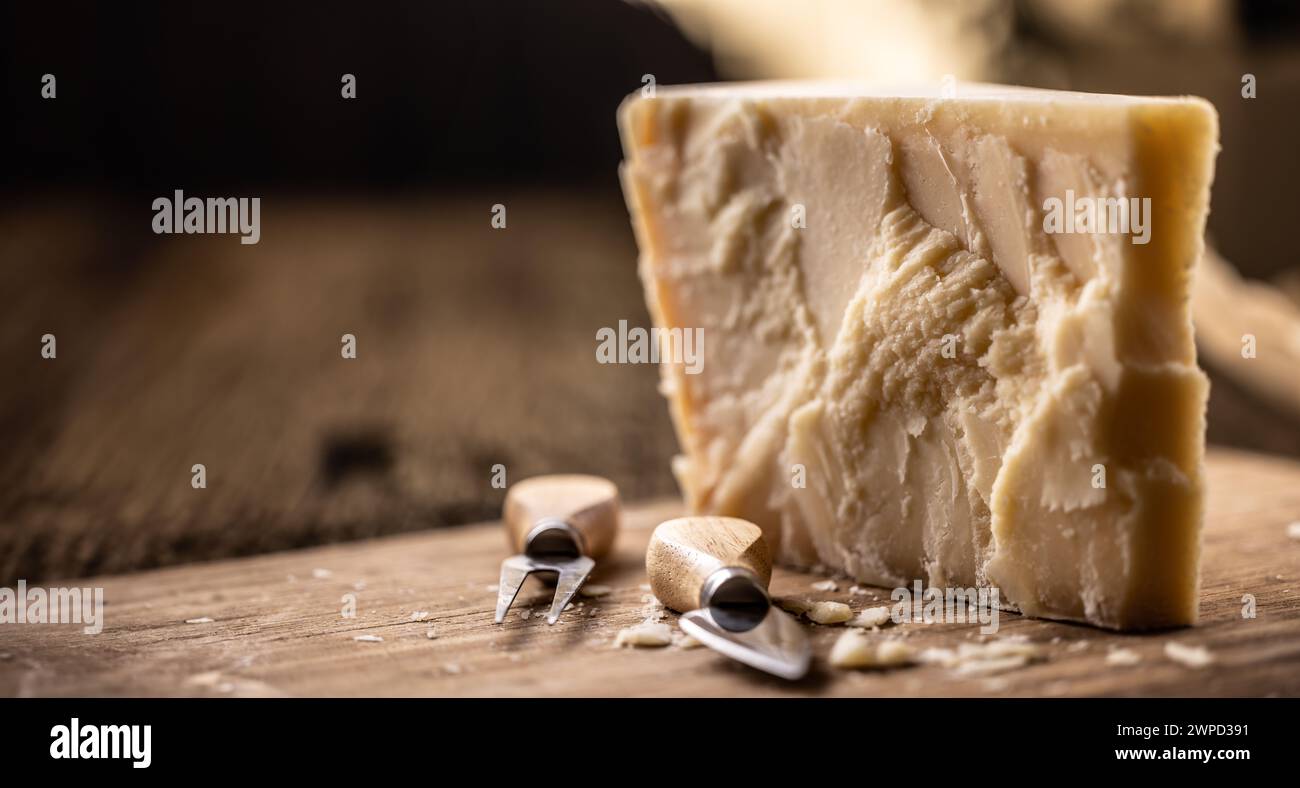 A block and pieces of Parmesan cheese on a cutting board along with a ...