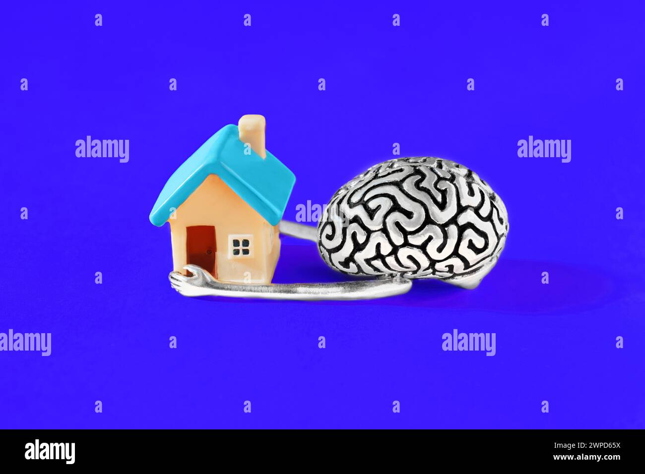 Human brain model grasping a toy house in its hands isolated on blue ...