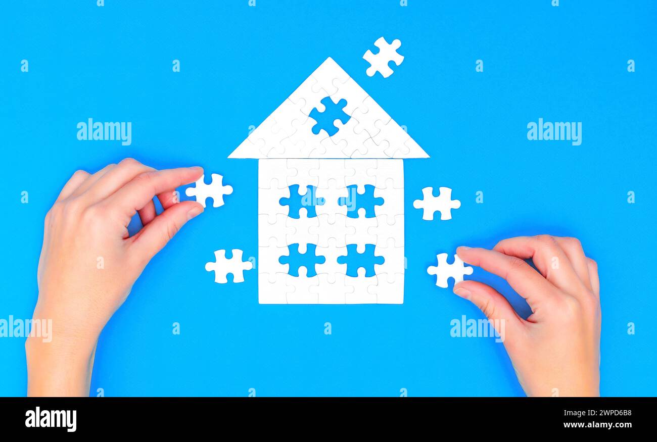 Close-up vie of female hands piecing together a house-shaped puzzle ...