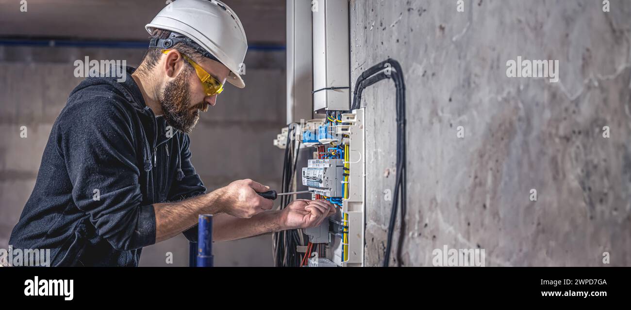 A male electrician works in a switchboard with an electrical connecting ...